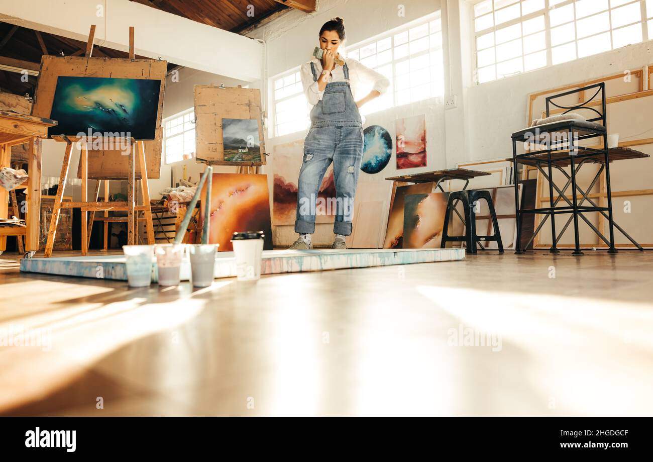 Thoughtful female painter looking at her painting on the floor ...