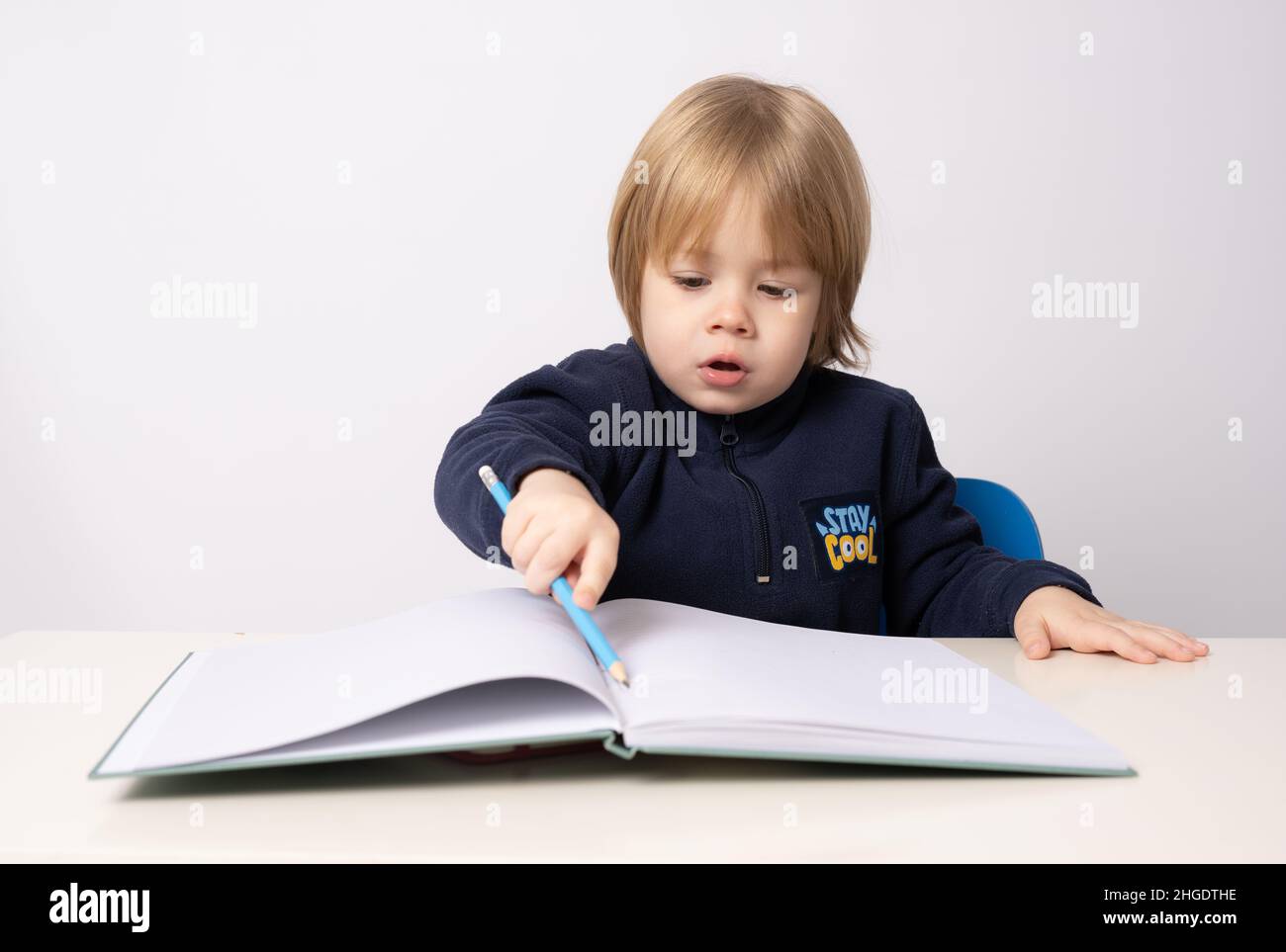 Little boy sitting at the table and drawing on a white background Stock ...