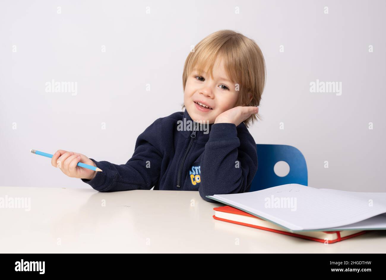 Smiling little boy sitting at the table isolated over white background ...