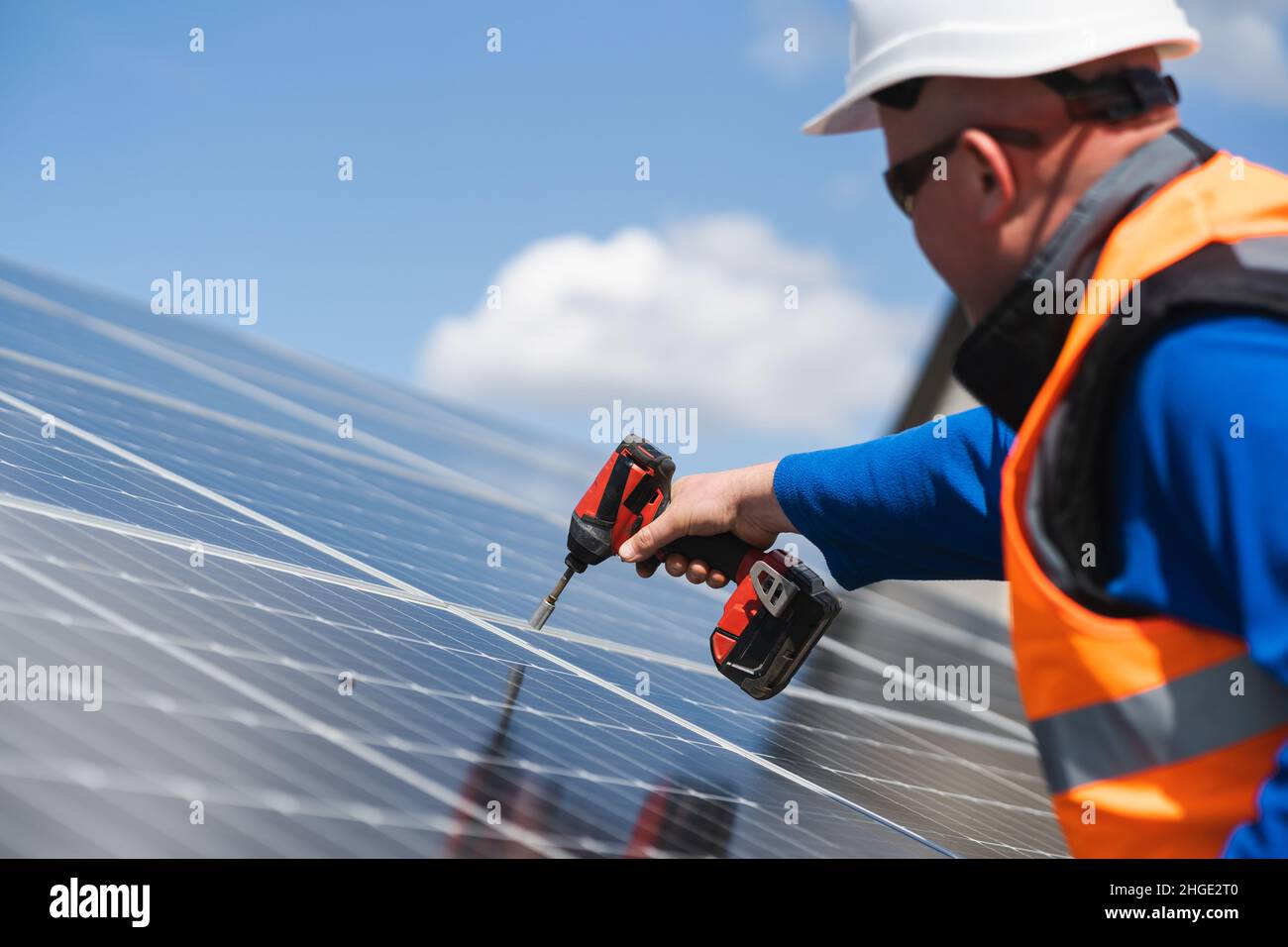 Worker with a drill-screwdriver to fix the panel of a solar power plant ...