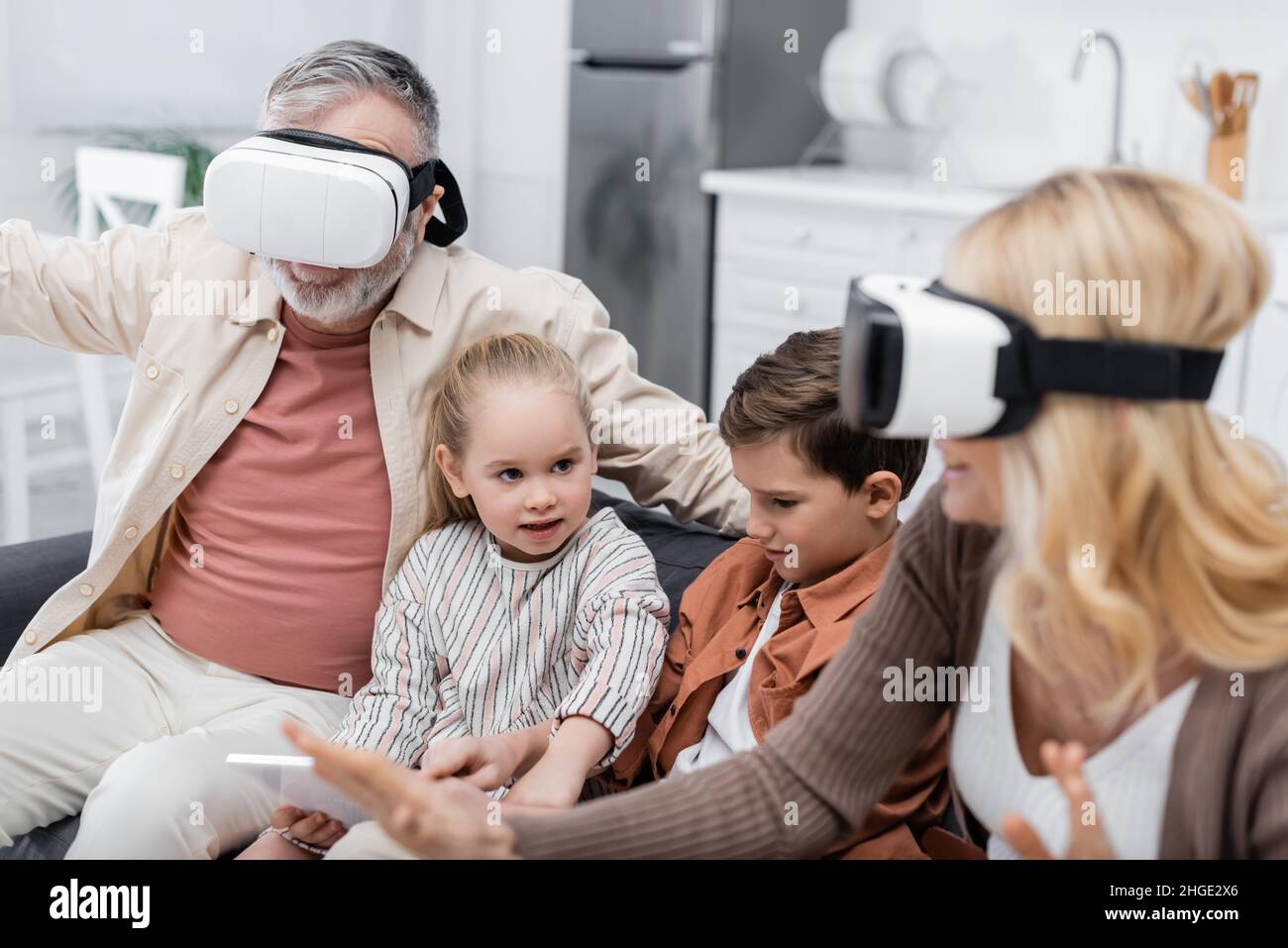 kids sitting on sofa with digital tablet near grandparents gaming in vr ...