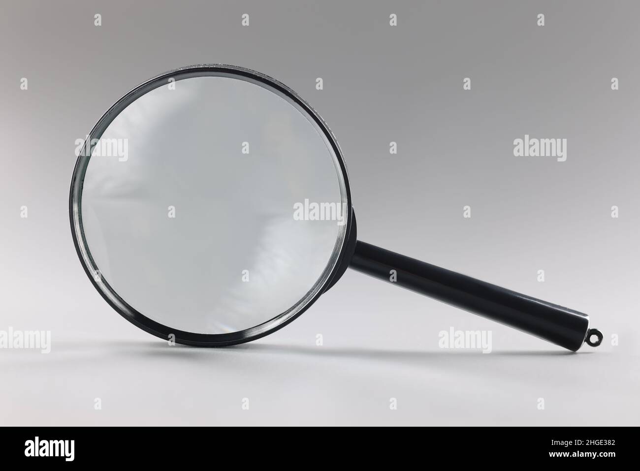 Single magnifying glass with black handle, leaning on grey surface ...