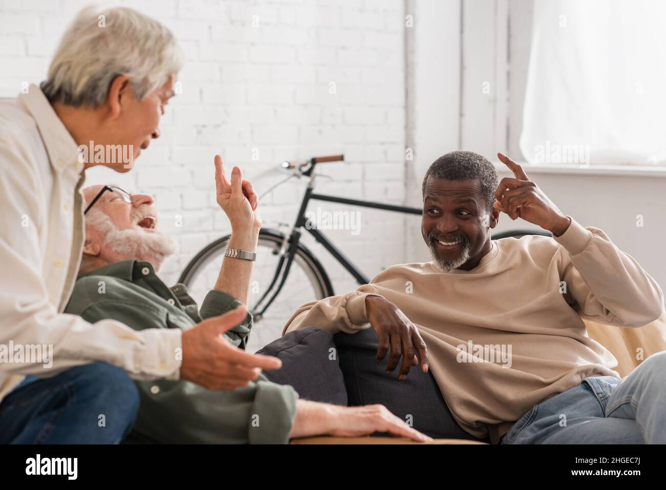 Cheerful multicultural elderly men talking on couch at home Stock Photo ...