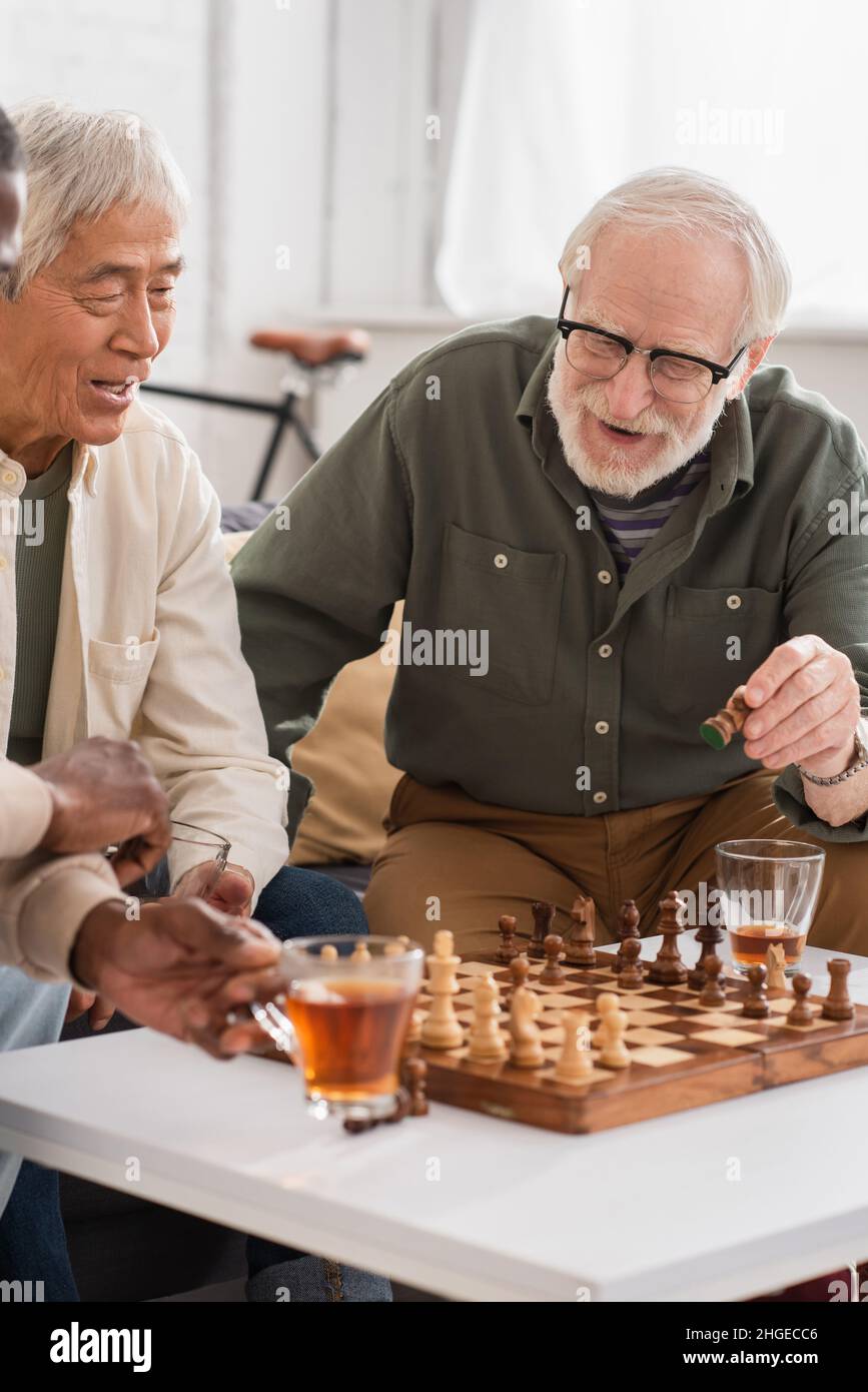Positive multiethnic friends playing chess near tea at home Stock Photo ...