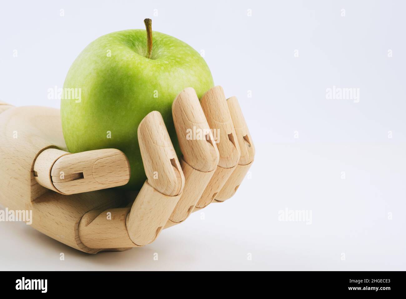 A wooden hand holding a granny smith apple on a white background Stock ...