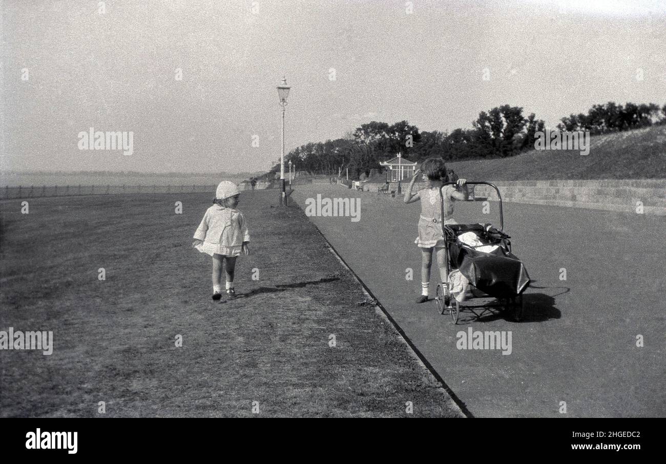 1930s, historical, at the coast, a young giril wlking pushing a small ...