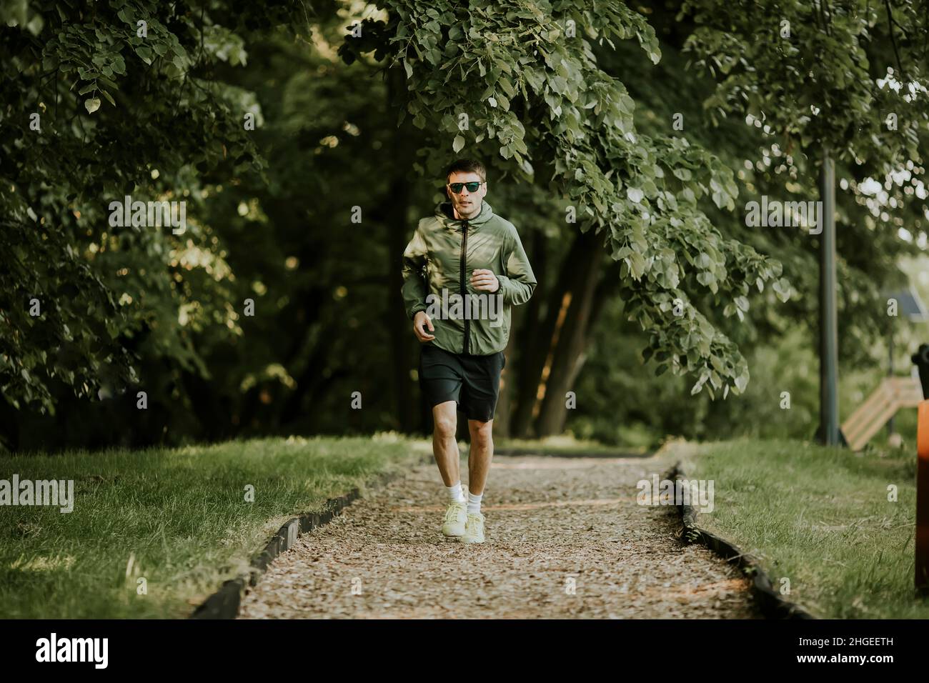 Handsome athletic young man running while doing workout in sunny green ...