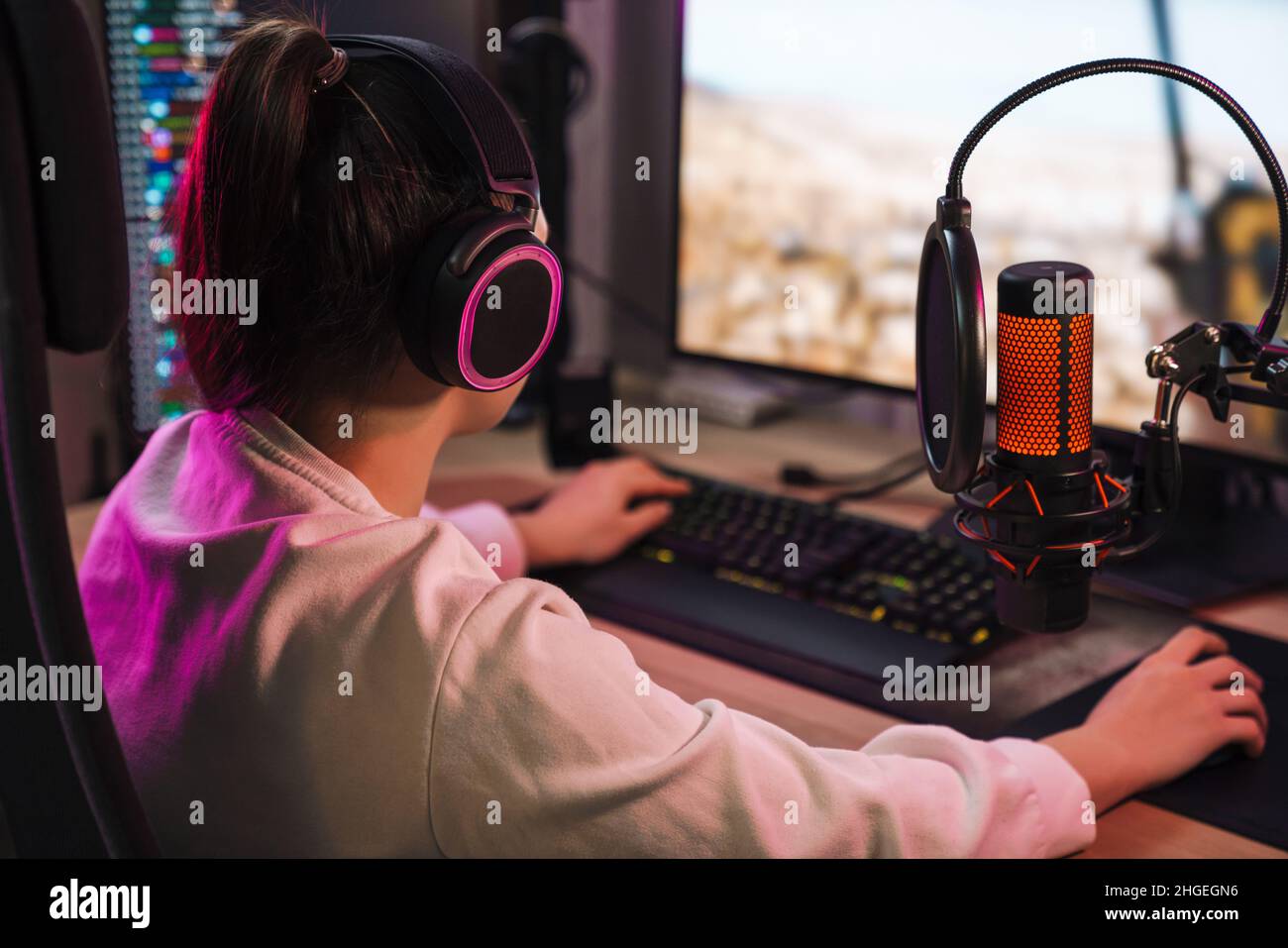 Back view of a young woman streamer gamer in headphones playing online ...
