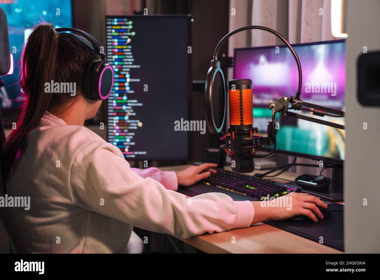 Back view of a young woman streamer gamer in headphones playing online ...