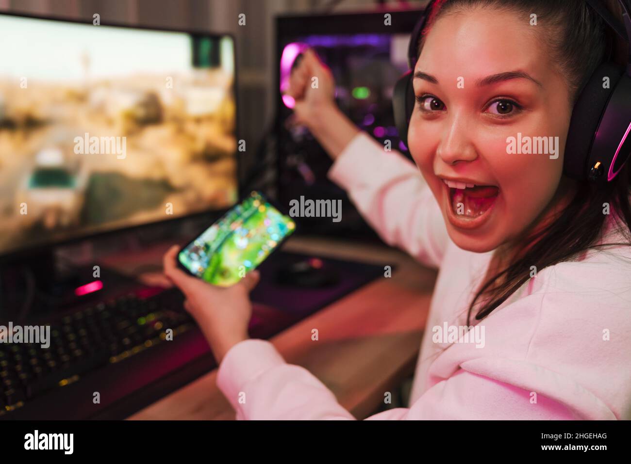 Young happy woman gamer playing video games on smartphone and computer ...