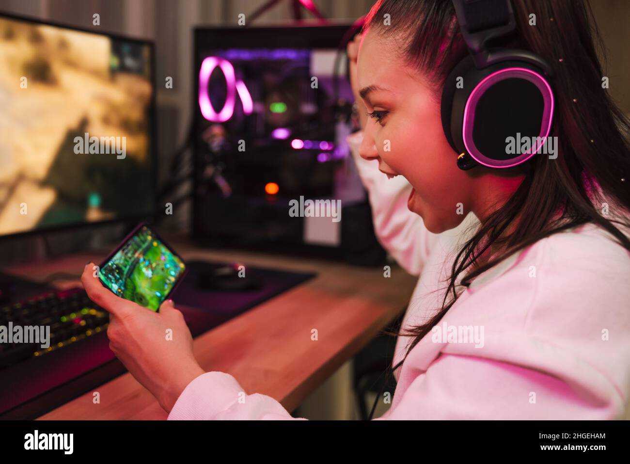 Young happy woman gamer playing video games on smartphone and computer ...