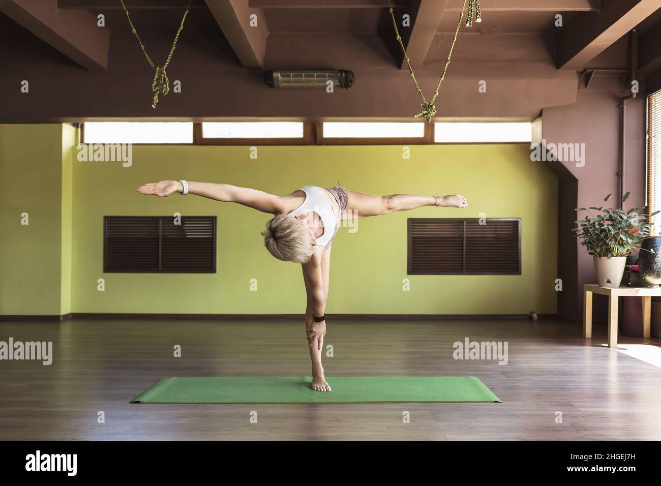 Blonde woman practicing yoga performs variation of Ardha chandrasana ...