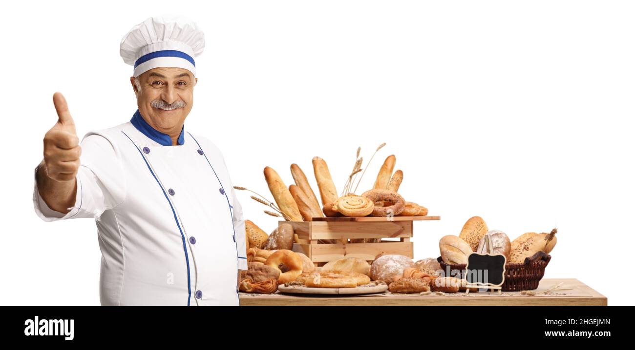 Mature male baker posing in front of a table with breads and gesturing ...