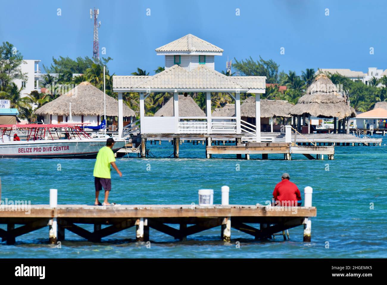 2 Belizean men fishing on a dock in San Pedro, Belize. A boat and ...