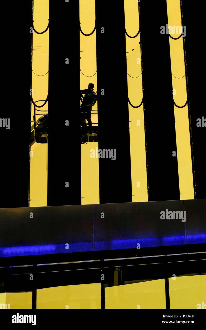 Construction worker silhouetted on the facade of Outernet complex at St ...