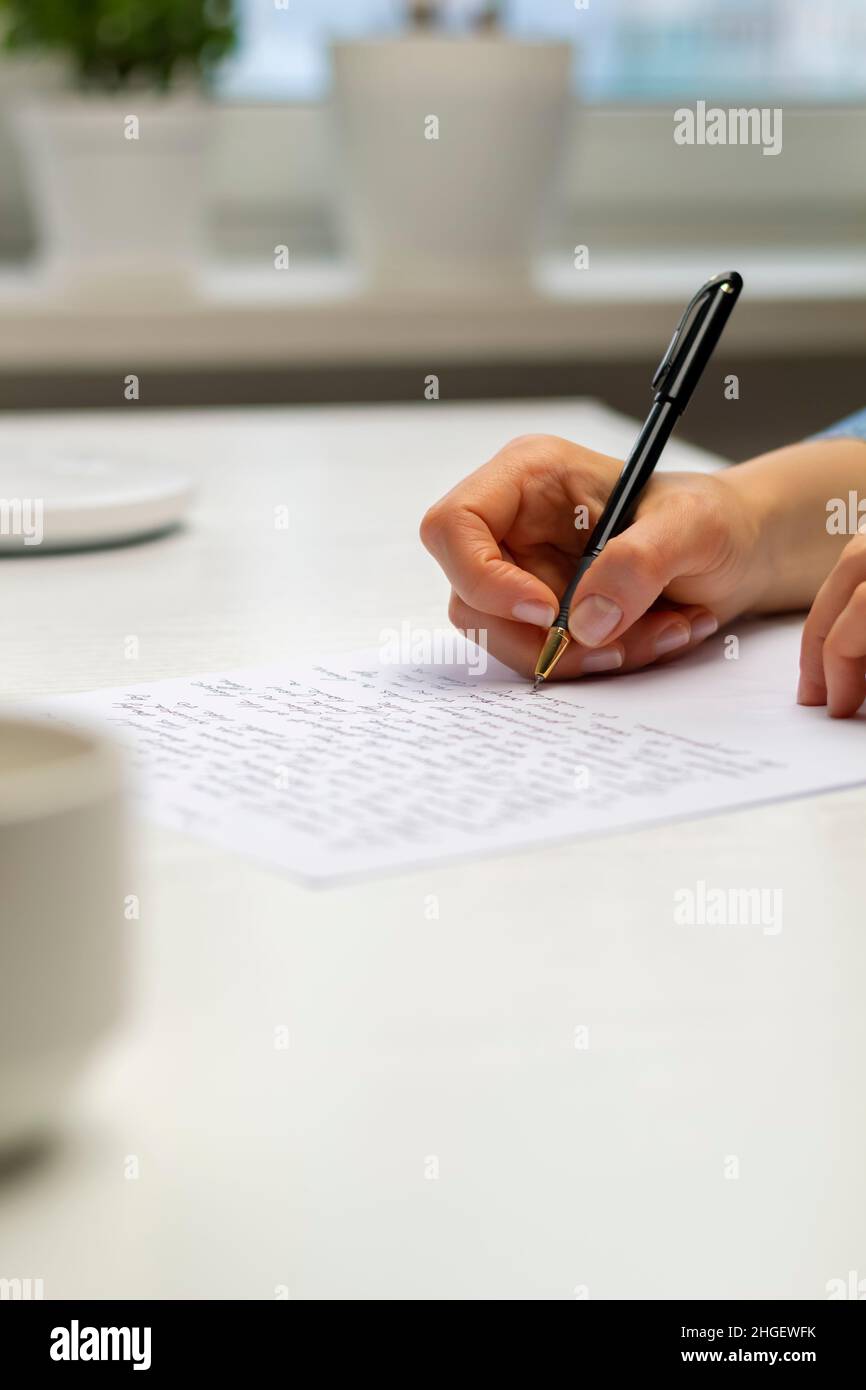 The woman writes a letter. Cropped hands on the table with pen and ...