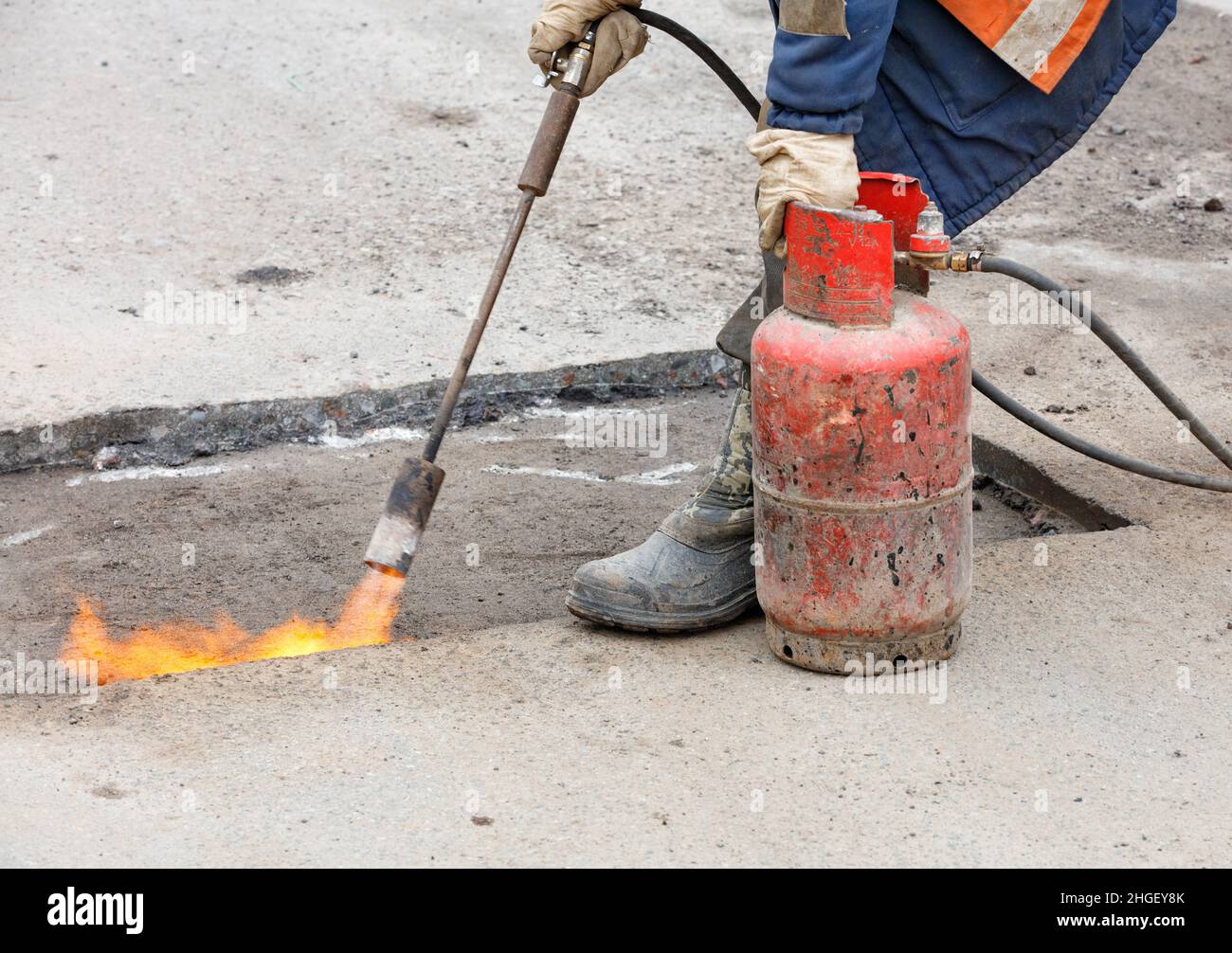 Pothole repair of the road. The worker, using a gas burner and a ...