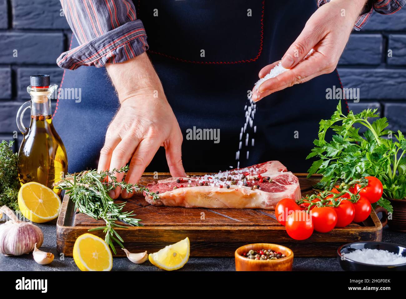 male chef is sprinkling salt over a porterhouse beef steak on ...