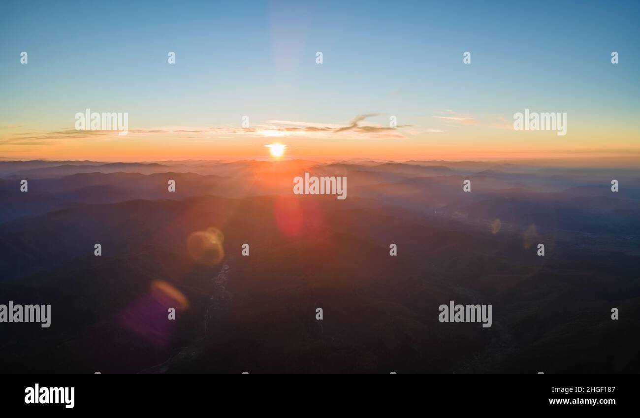 Aerial view of dark mountain hills with bright sunrays of setting sun ...