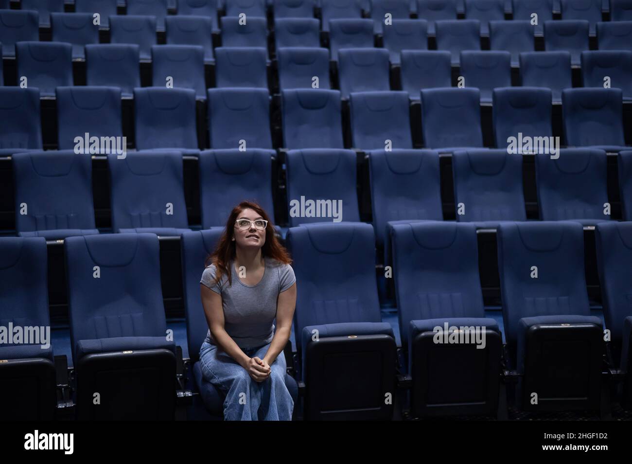 Caucasian red-haired woman sits on the front row in a cinema in an empty hall. The girl is ...