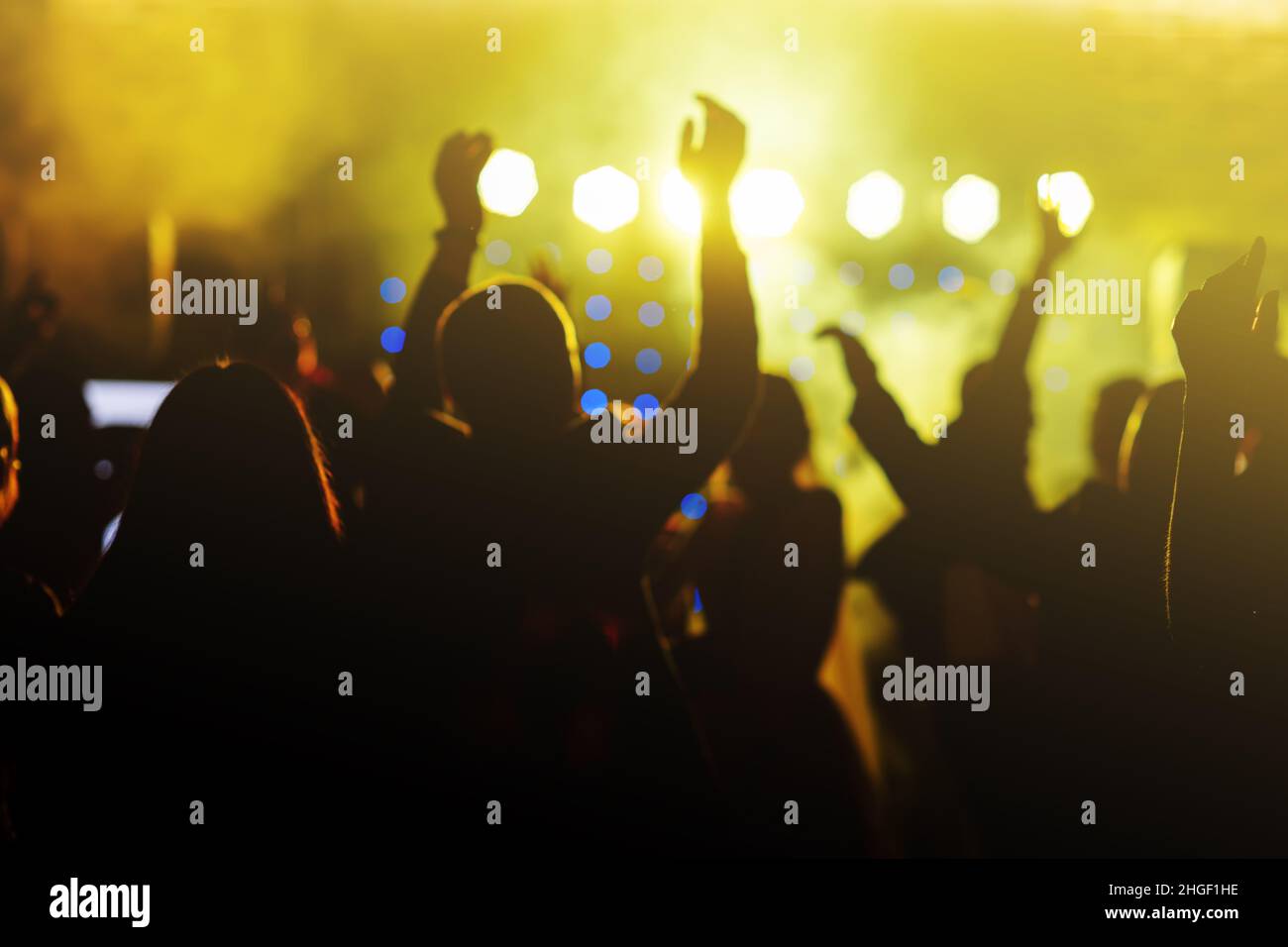 cheering crowd in front of bright yellow stage lights. Silhouette image ...
