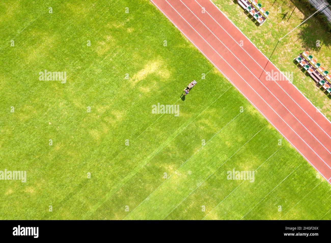 Aerial view of small figure of worker cutting green grass with mowing ...