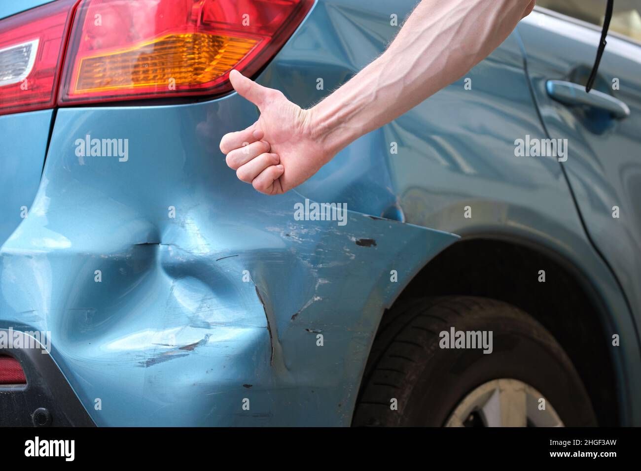 Driver hand examining dented car with damaged fender parked on city ...