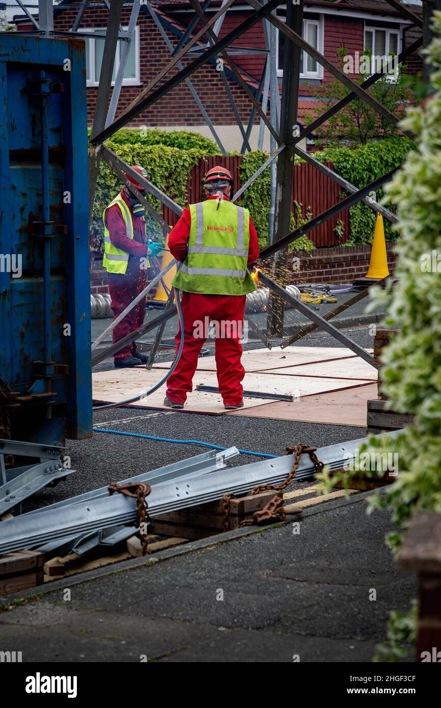Workmen in PPE use oxy acetylene torches to cut out damaged parts of a ...