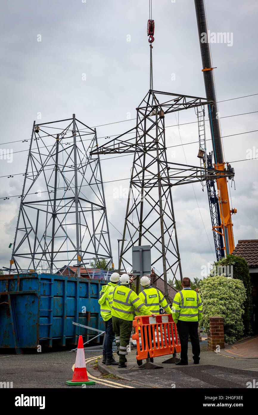 Technicians watch the top half of an electricity pylon being lowered to ...