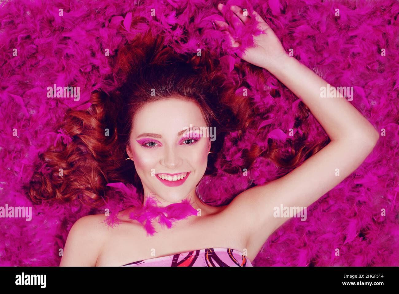 Happy brunette is smiling. Girl lies on a background of purple feathers ...