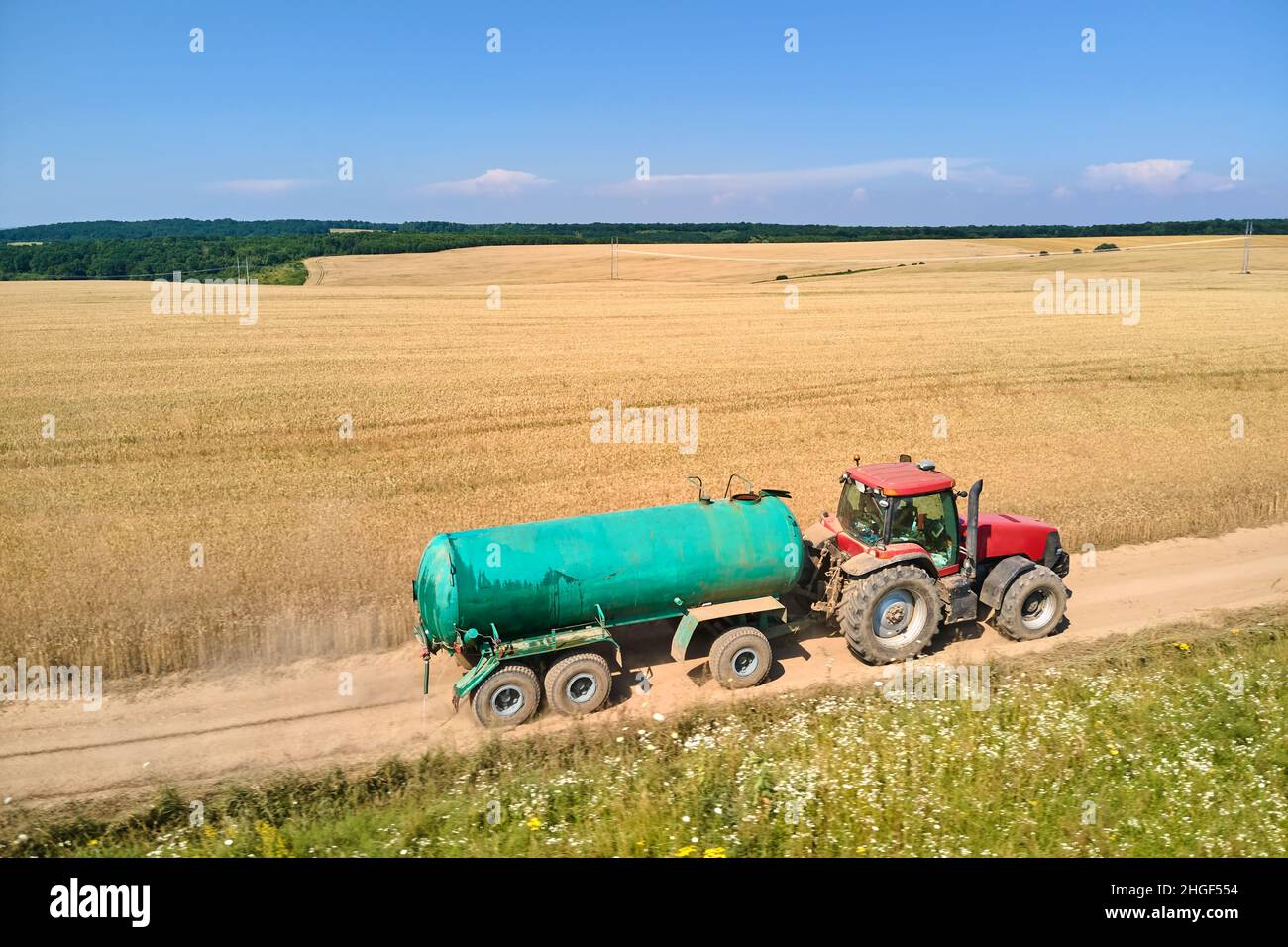 Tractor with water tank trailer driving on dirt road between ...