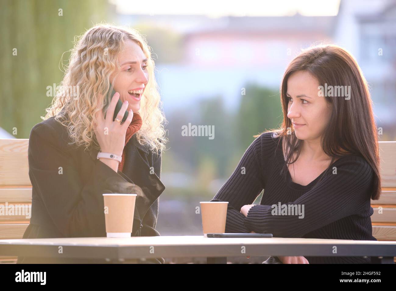 Unhappy young woman waiting angrily while her friend is talking happily ...