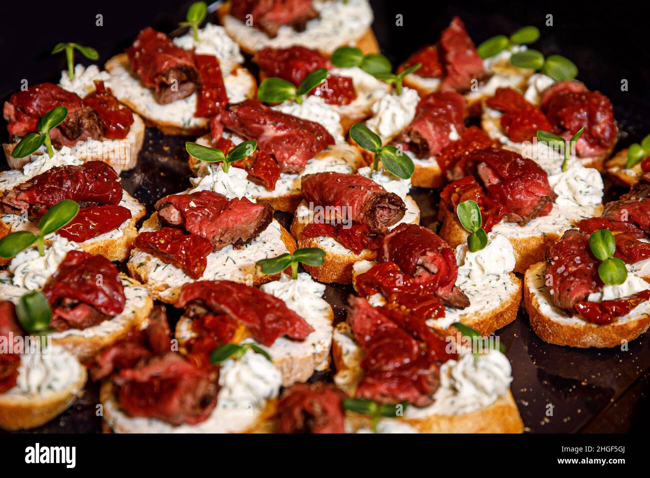Meat bruschetta on a black tray. Beef and dried tomato on a baguette ...