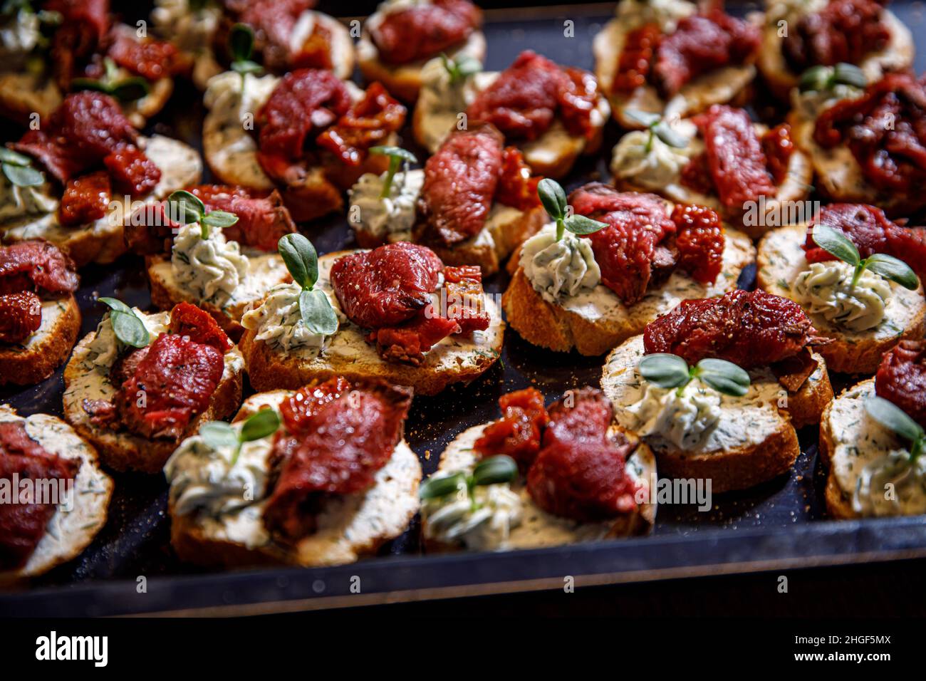 Meat bruschetta on a black tray. Beef and dried tomato on a baguette ...