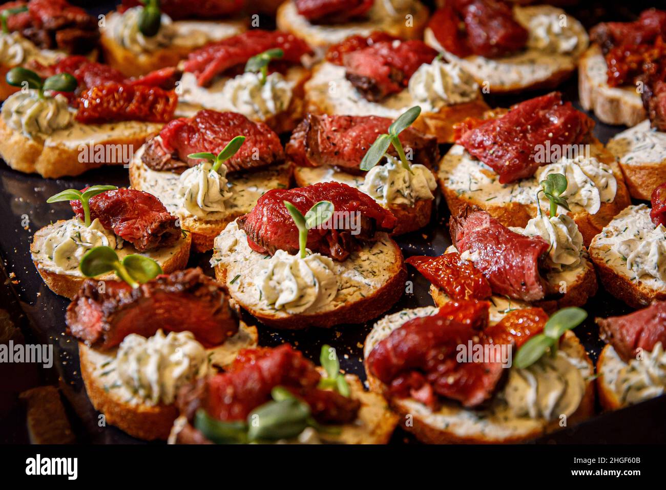 Meat bruschetta on a black tray. Beef and dried tomato on a baguette ...