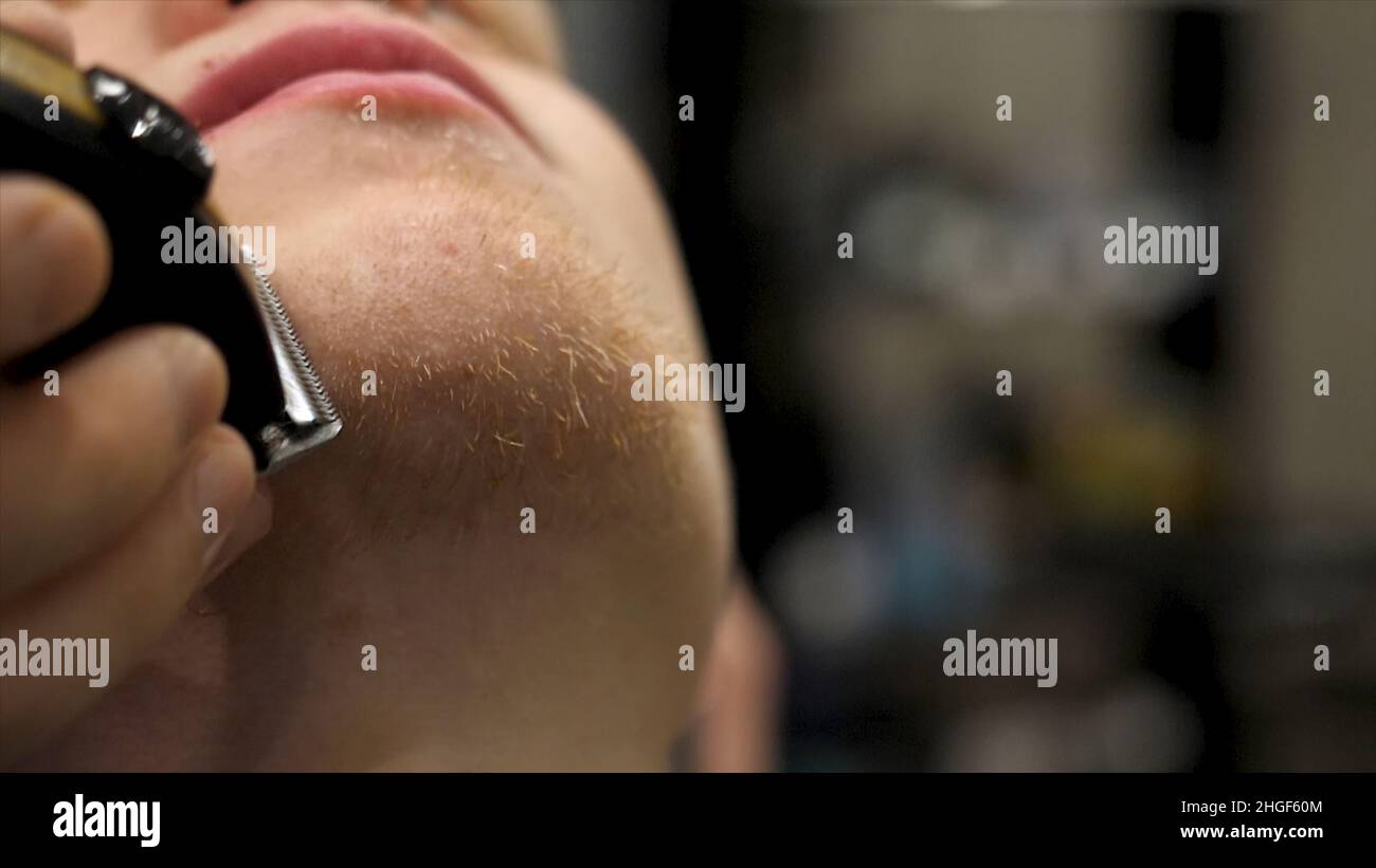 Close-up side view portrait of young bearded man getting beard grooming ...