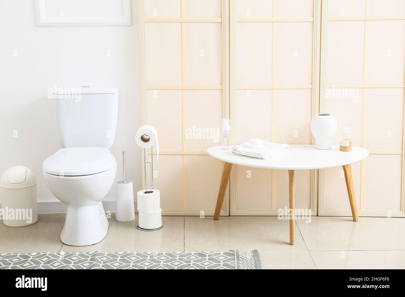 Toilet bowl, paper holder and table with bath supplies in restroom ...