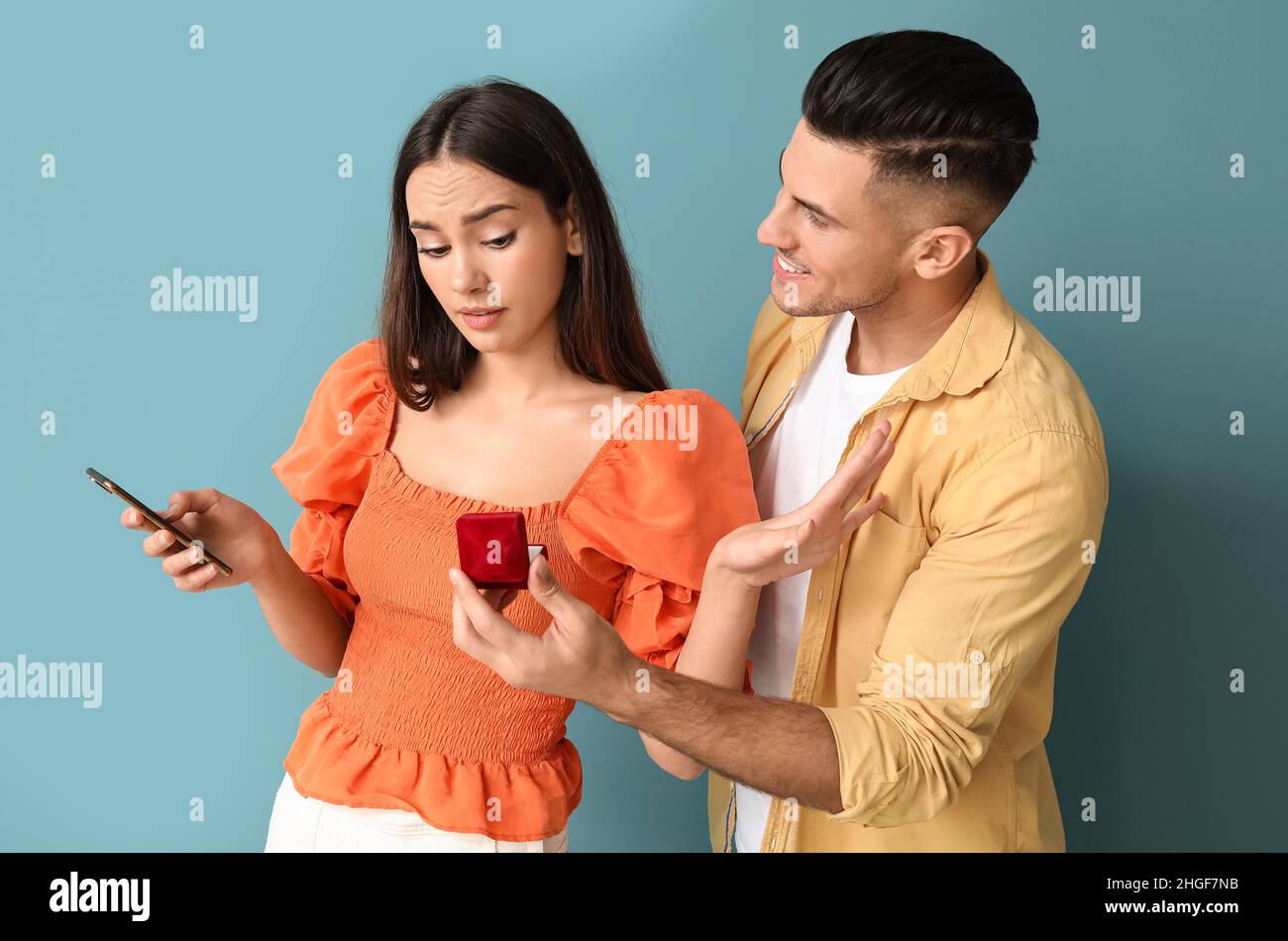 Young woman with phone rejecting marriage proposal on blue background ...