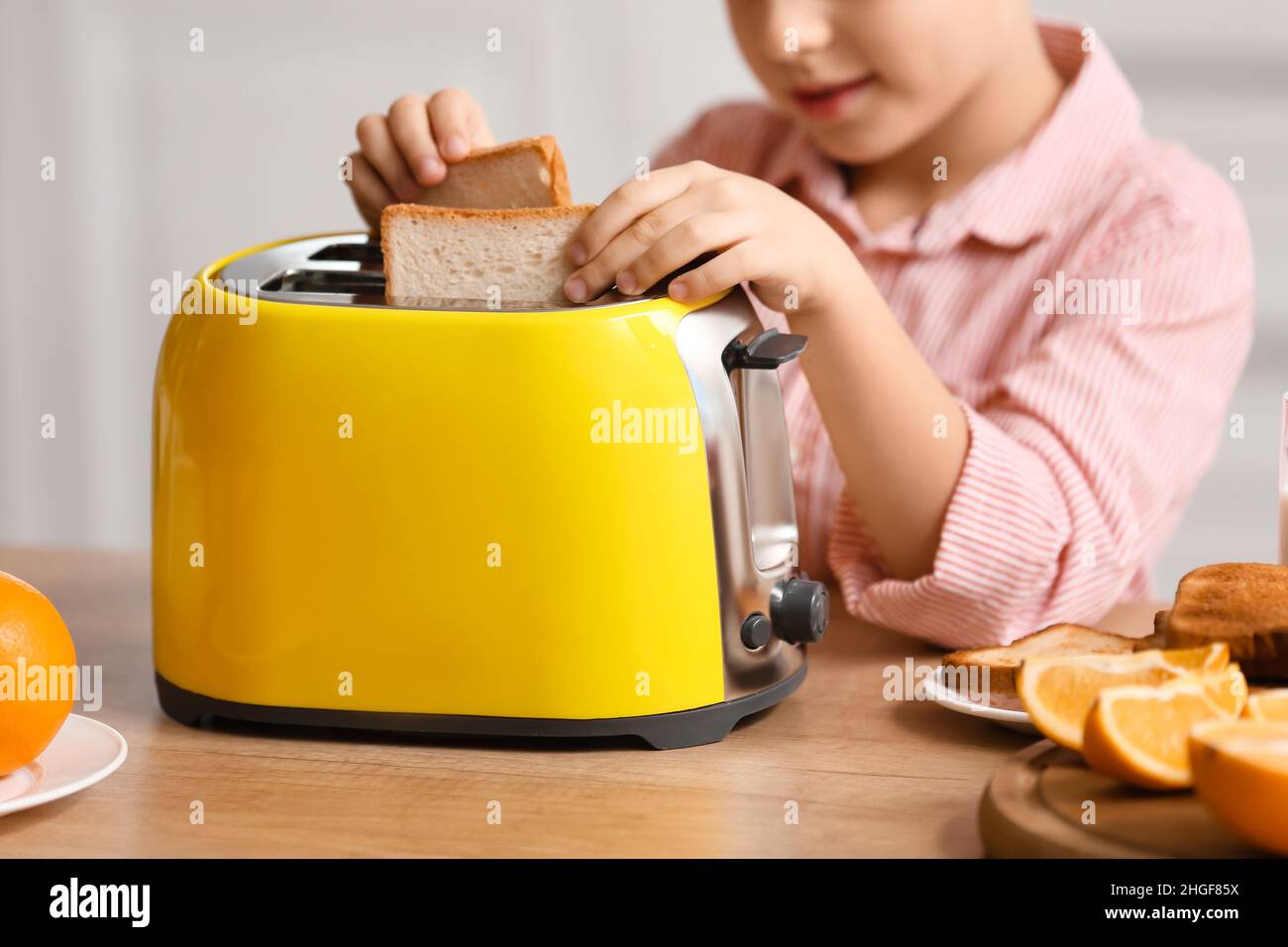 Little boy putting bread slices into yellow toaster in kitchen Stock ...