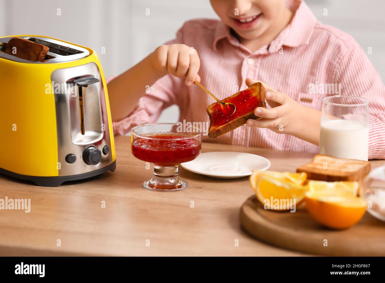 Cute little boy spreading jam onto toasted bread slice in kitchen Stock ...