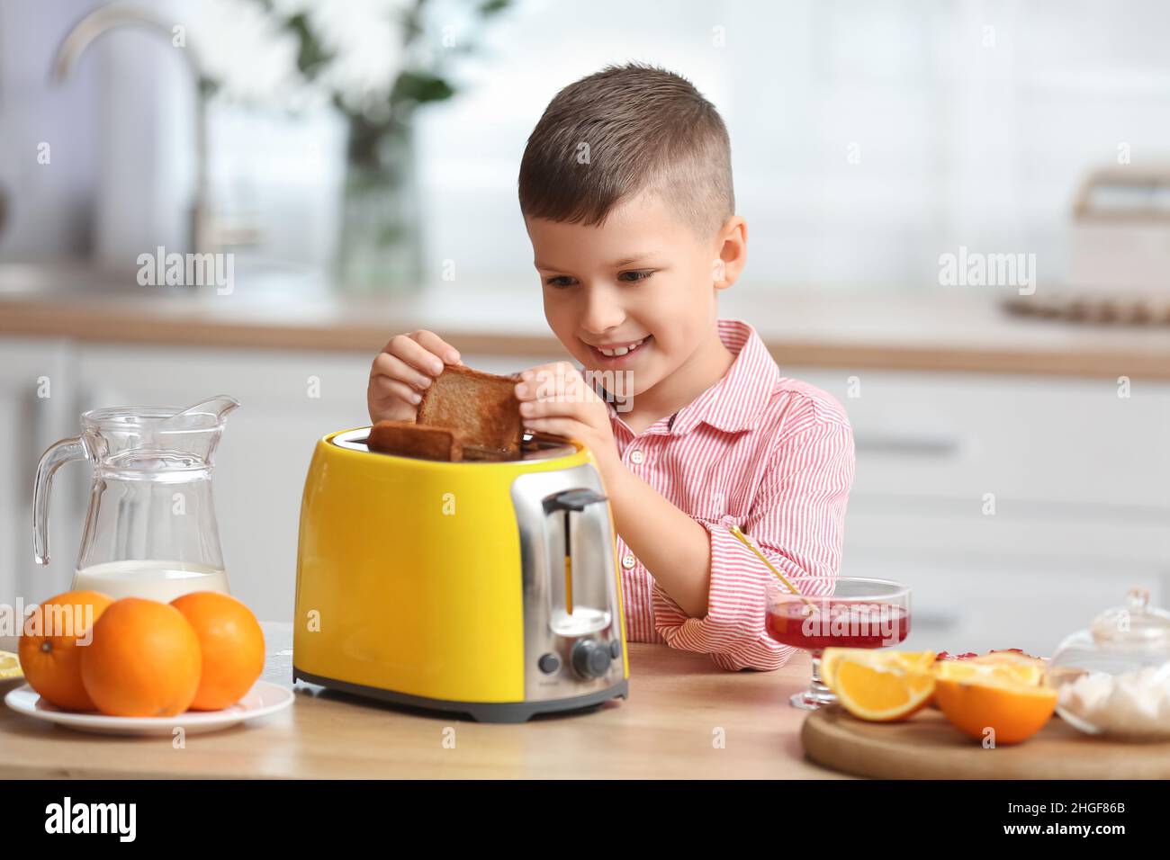 Cute little boy taking bread slice from yellow toaster in kitchen Stock ...