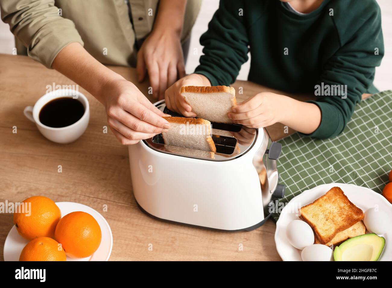 Little boy and his mother putting bread slices into toaster in kitchen ...