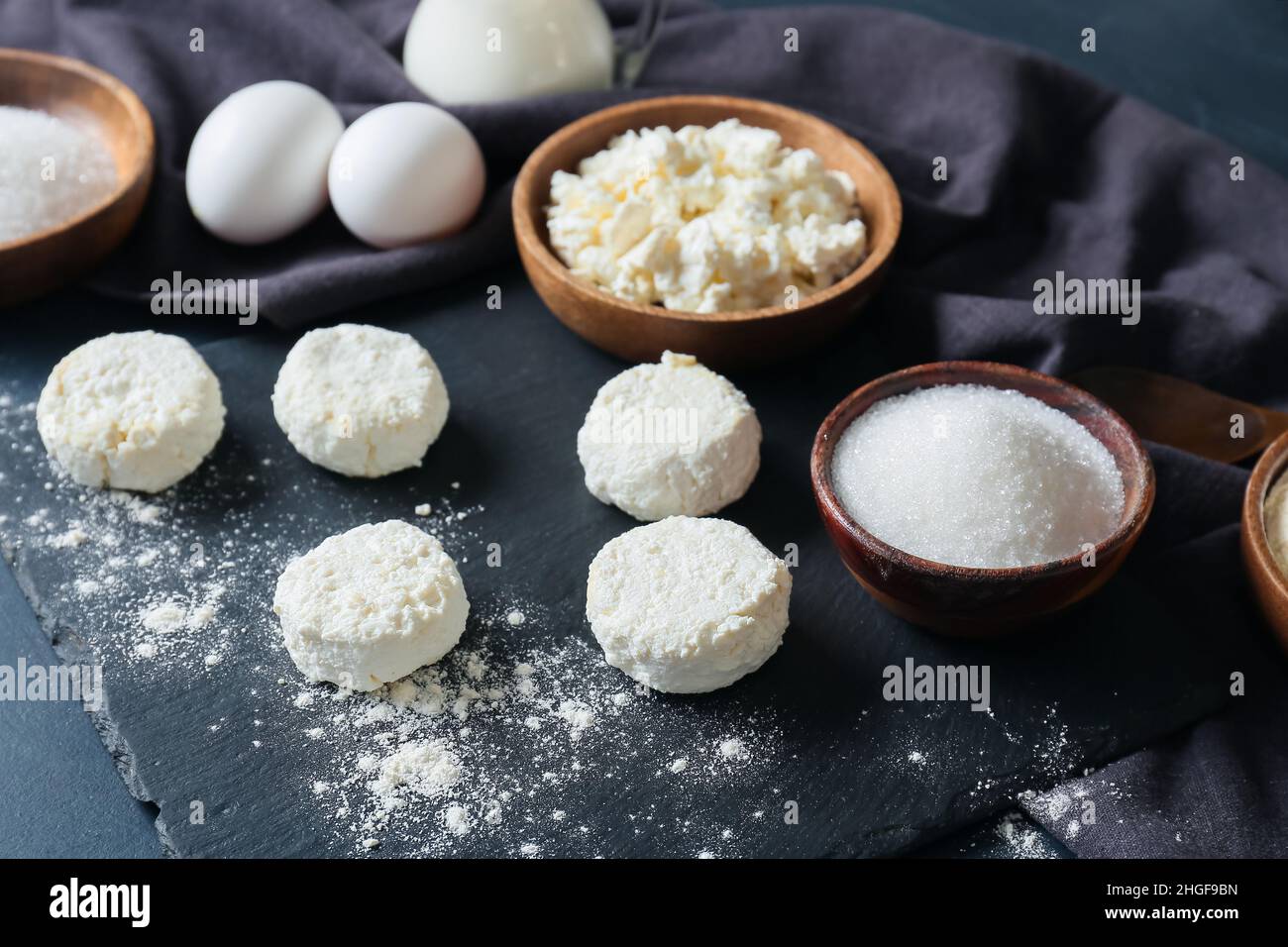 Board with uncooked cottage cheese pancakes and ingredients on black ...
