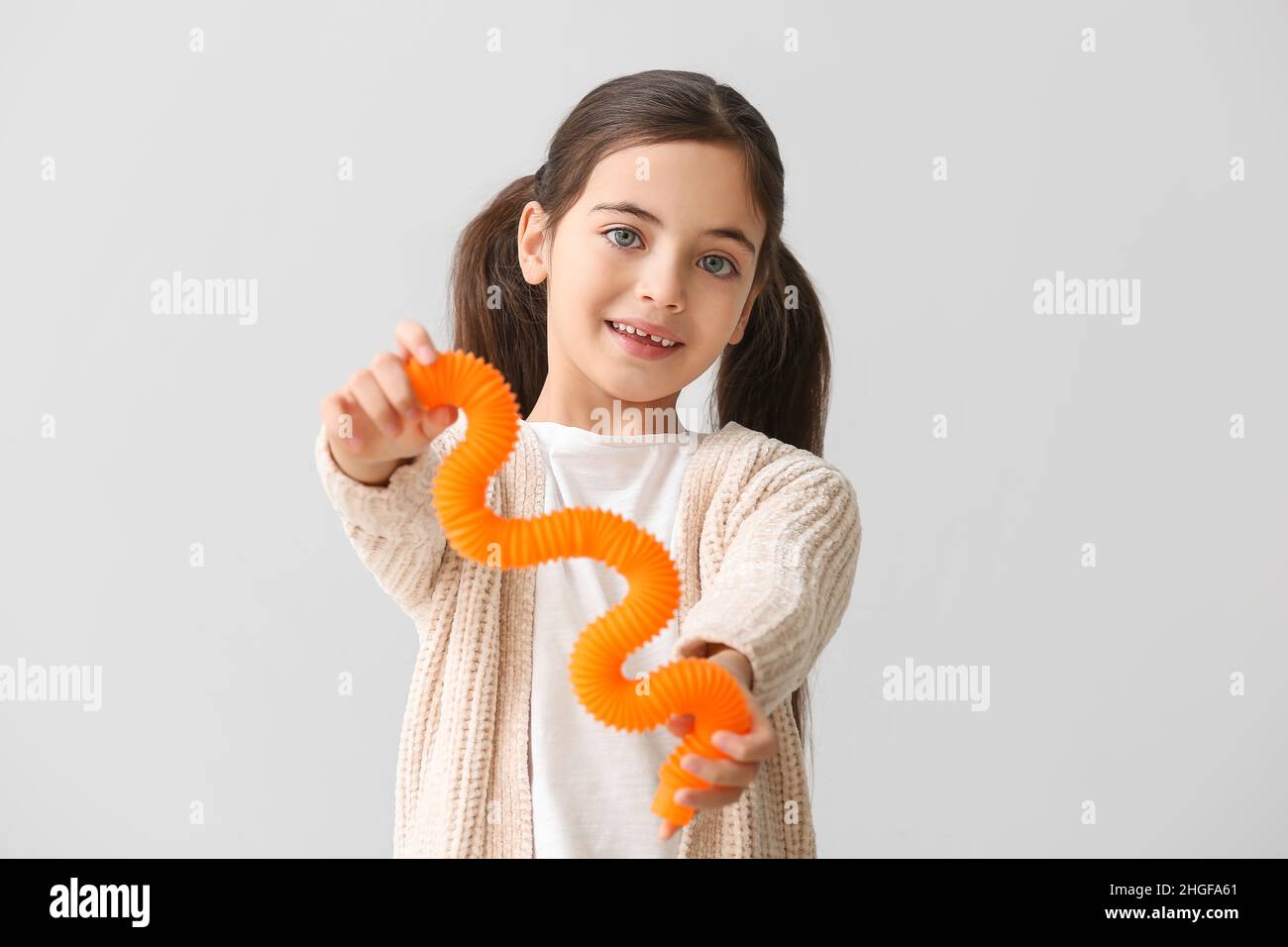 Little girl with orange Pop Tube on light background Stock Photo - Alamy