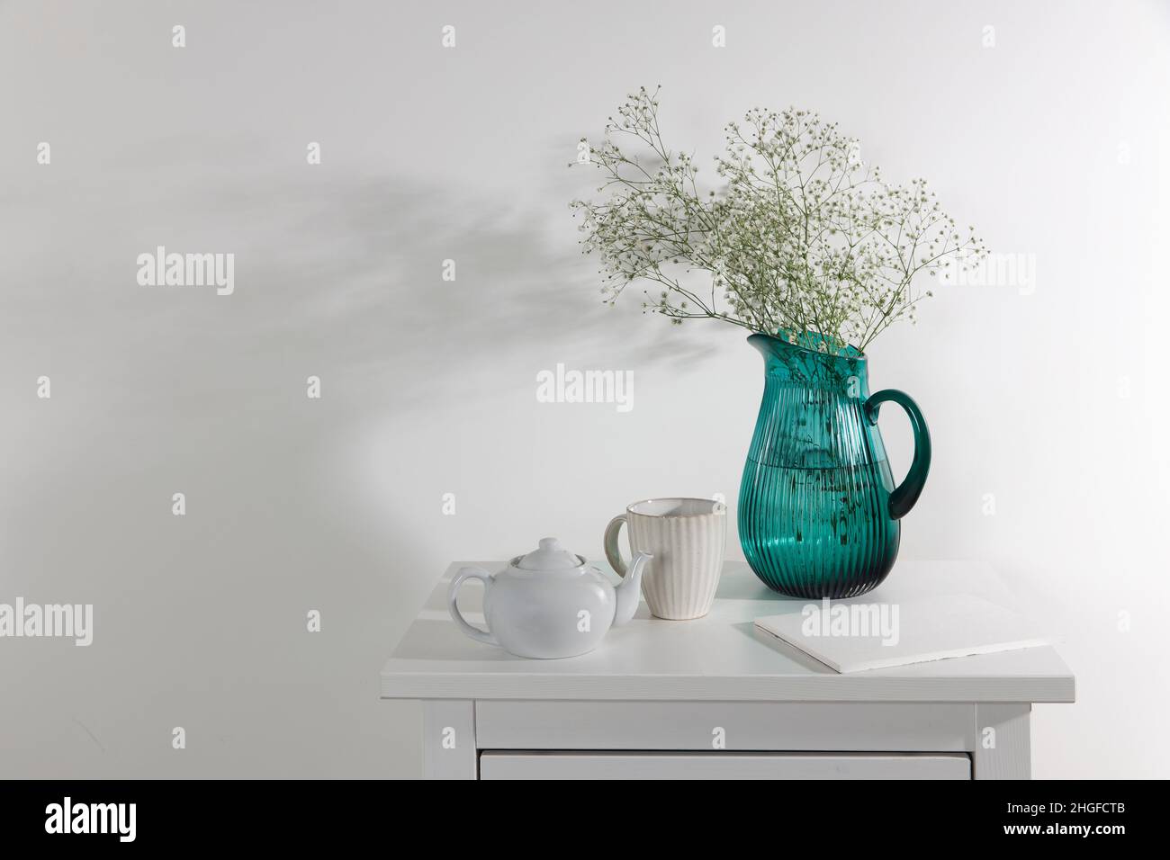 A large glass green jug with a bouquet of gypsophila, a white cup, a ...