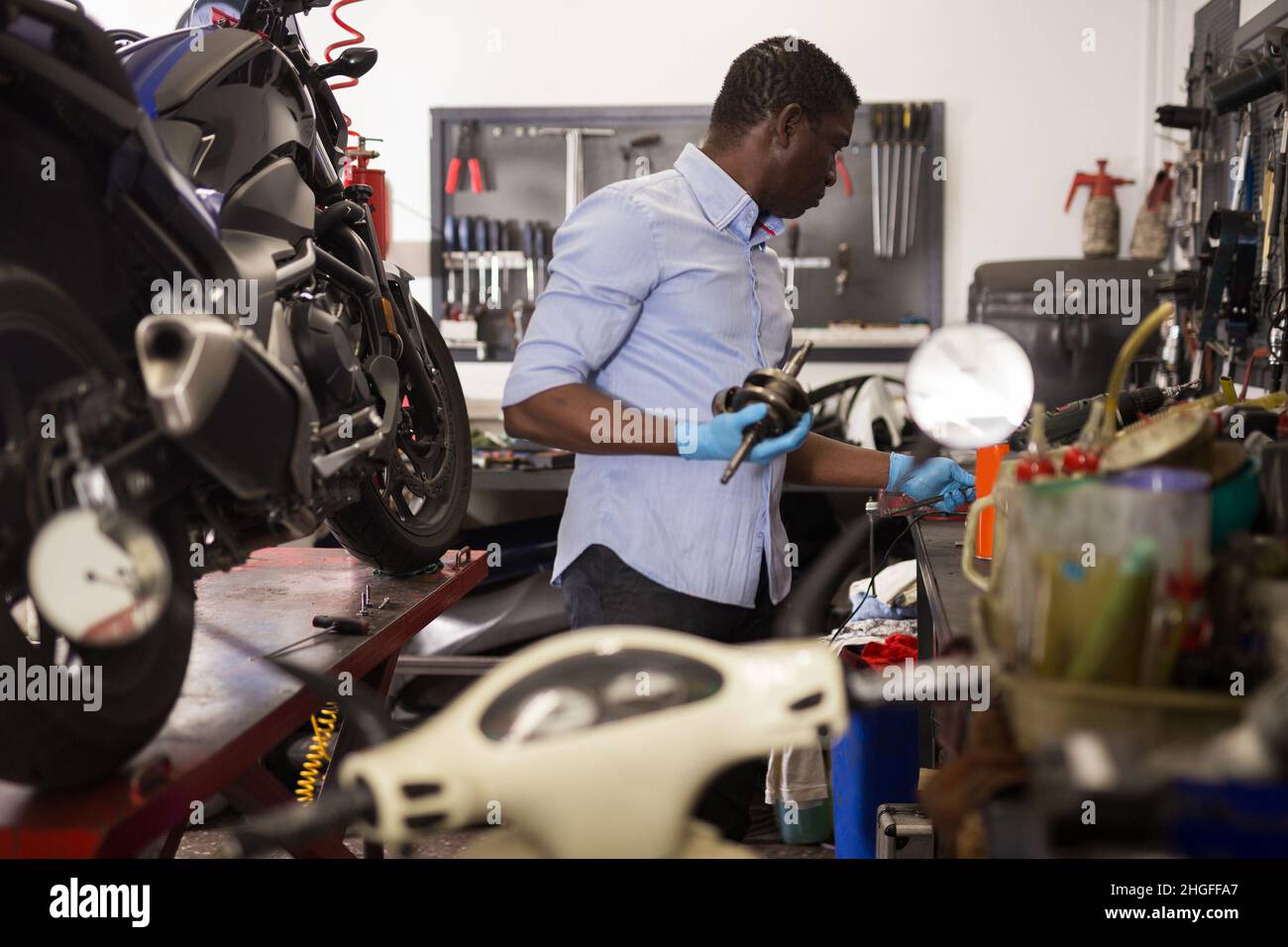 Confident worker examines a broken motorcycle part of the working area ...
