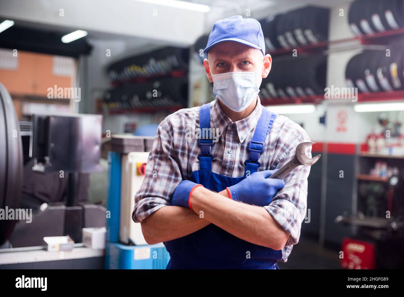 Workman in protective mask standing near car at auto repair service ...
