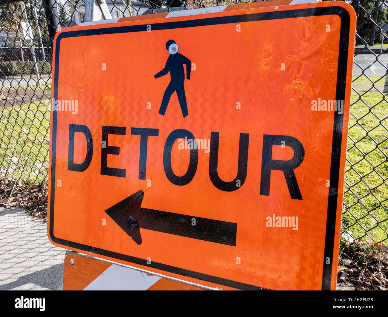 Angled view of an orange detour sign on a sidewalk near a construction ...