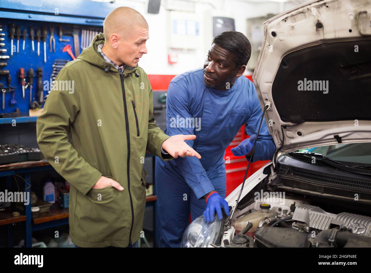 Worried client talking with specialist about repairing his car engine ...