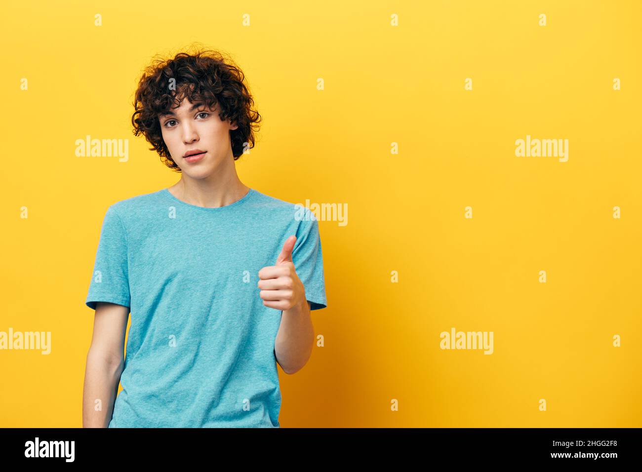 curly guy showing thumb up yellow background studio Stock Photo - Alamy